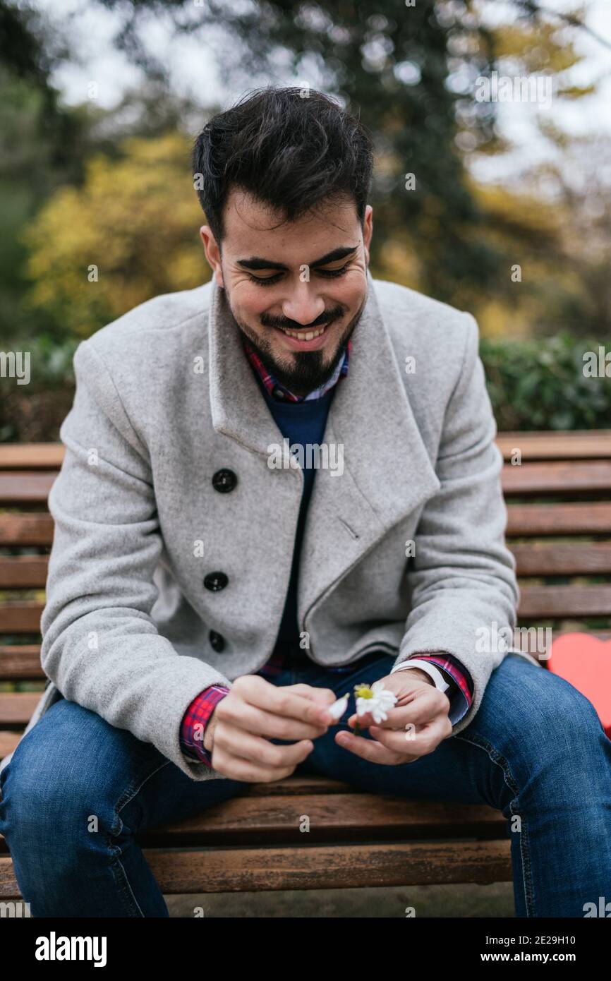 Young male plucking off the petals from a white flower while sitting on ...