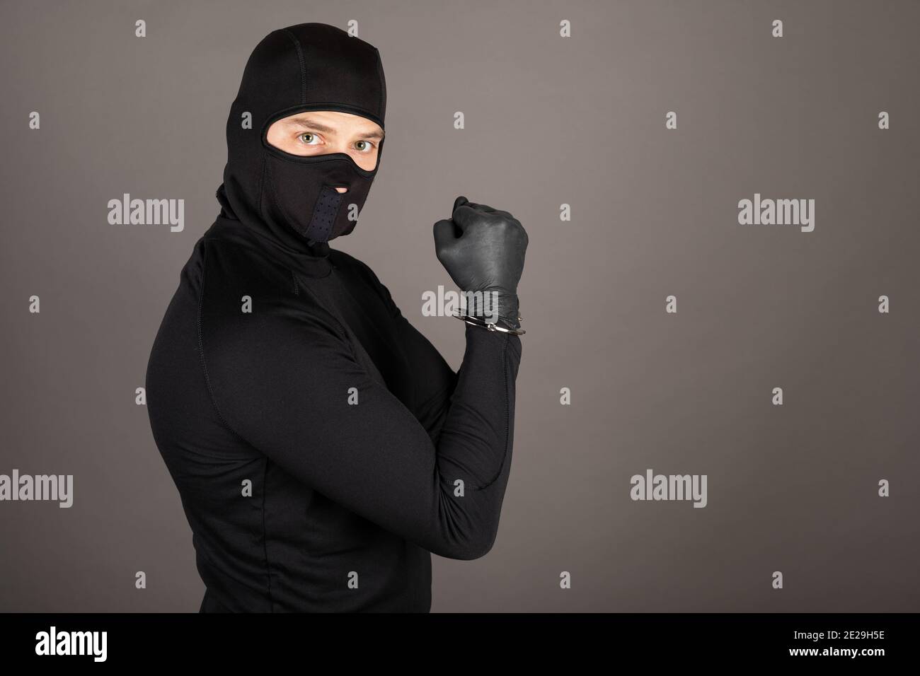 Thief dressed in black suit and having mask on his face is posing with ...