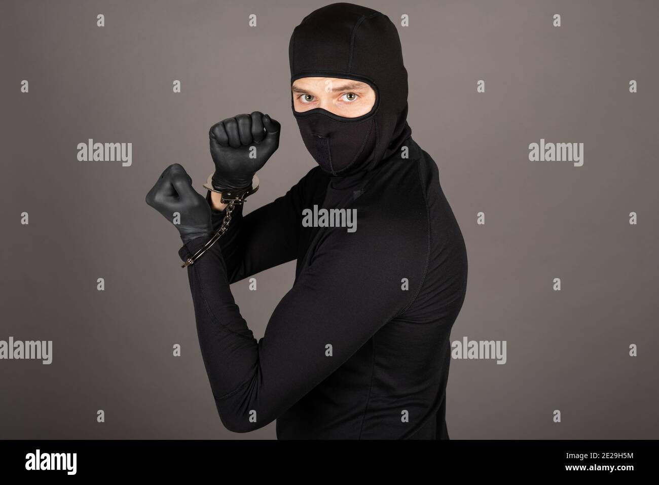 Thief dressed in black suit and having mask on his face is posing with ...