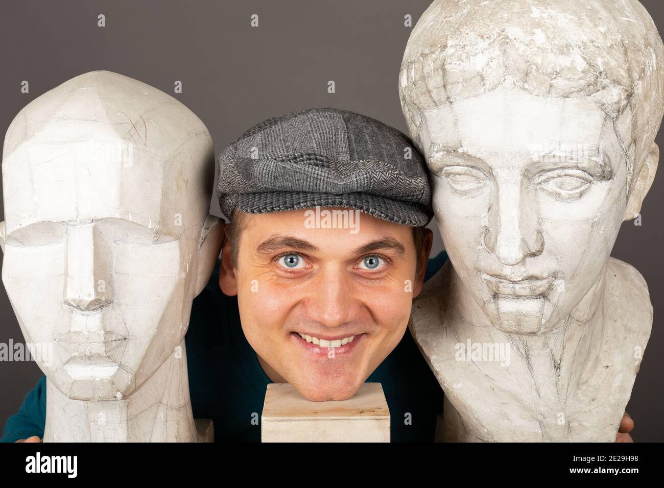 Portrait of a young creative male artist holding a gypsum statues head ...