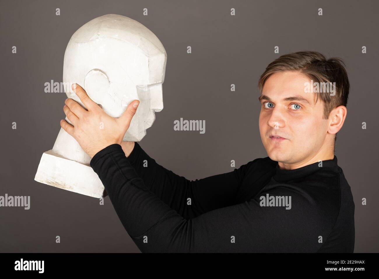 Portrait of a young creative male artist holding a gypsum statues head ...