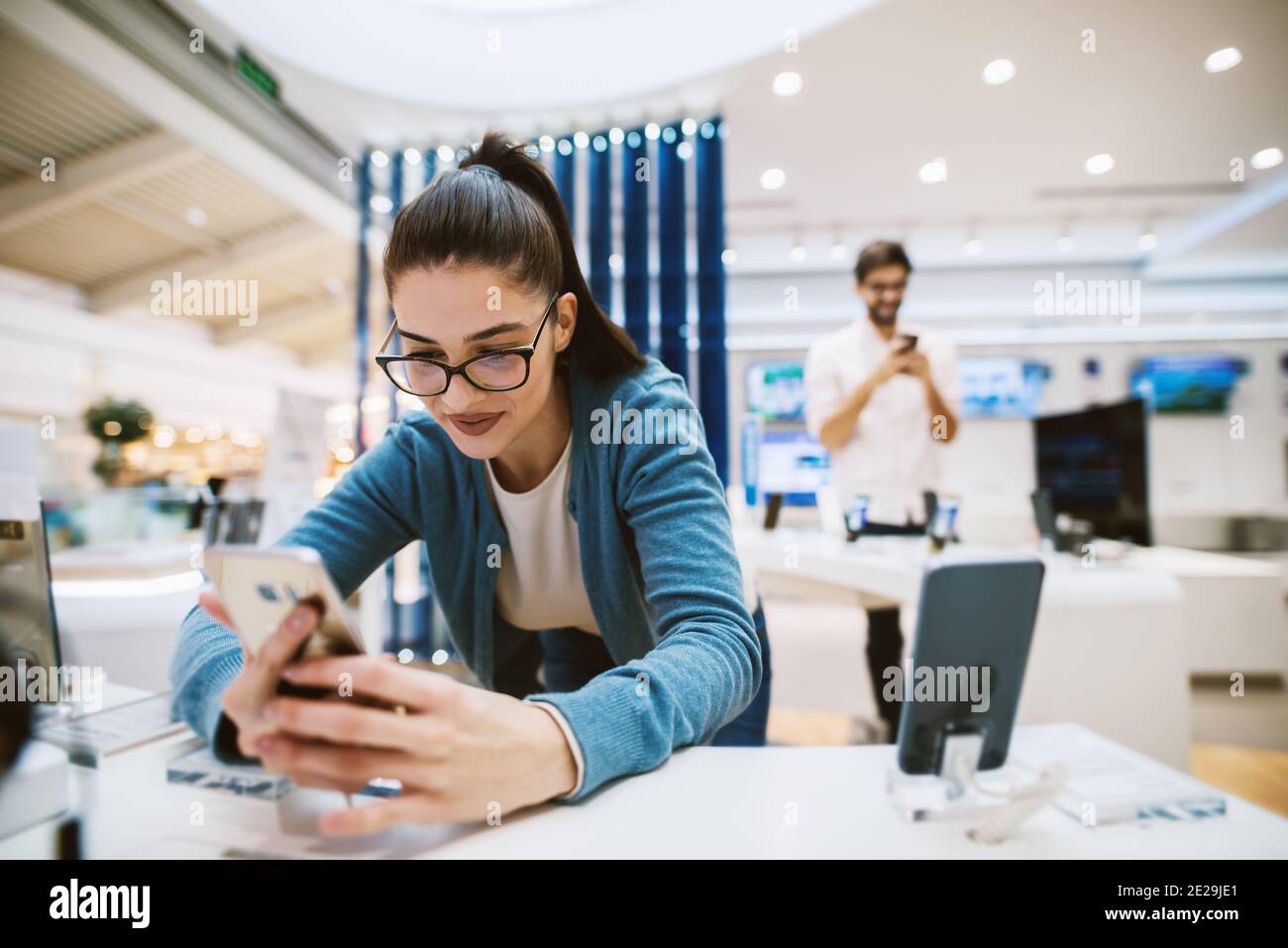 Beautiful modern girl is testing new telephone in tech store while her ...