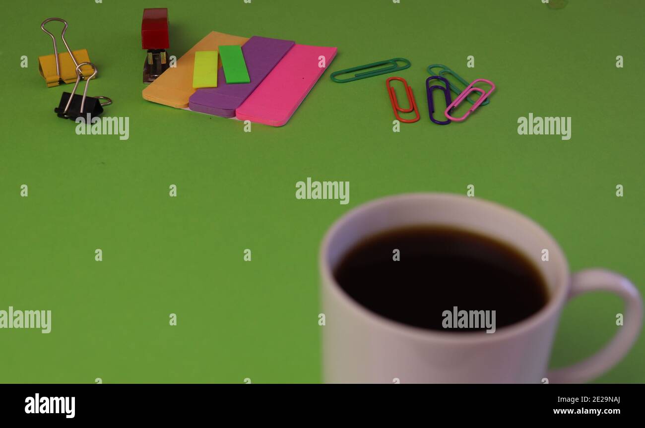 Cup of coffee, paper clips, stapler, and sticky notes on a green desk ...