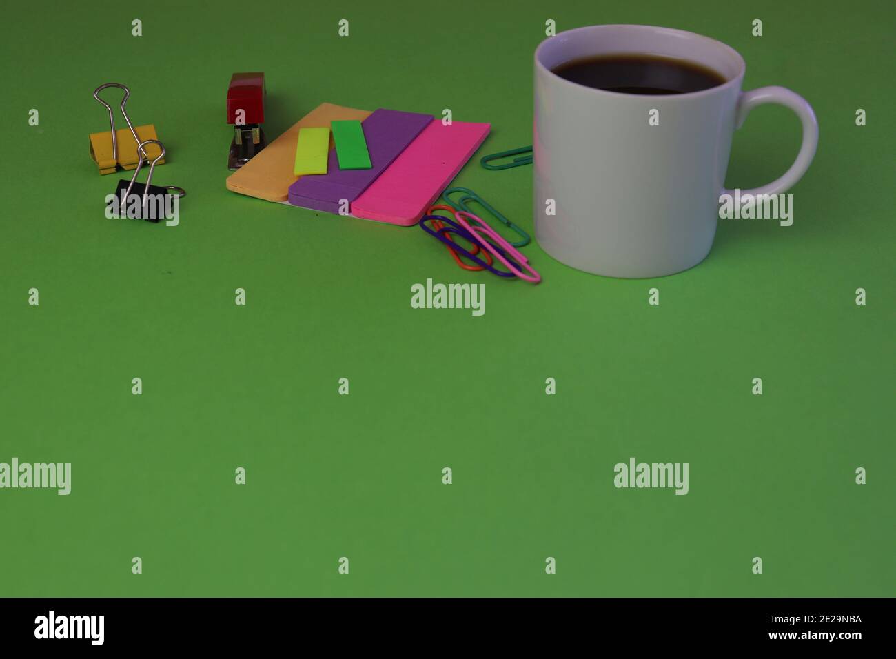 Cup of coffee, paper clips, stapler, and sticky notes on a green desk ...
