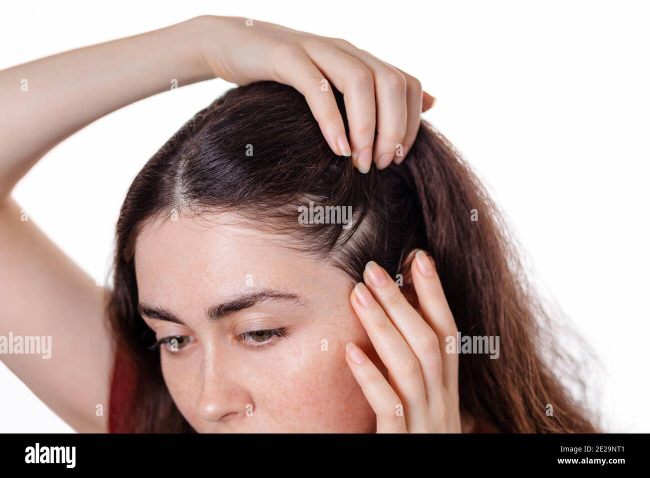A woman examines the parting in her hair, pushing the strands apart ...