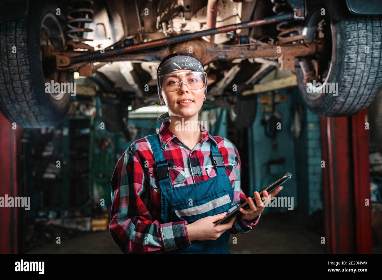 A young beautiful female mechanic, in a uniform and glasses, with a ...