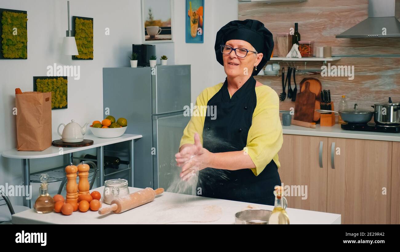 Happy old baker woman claping hands with flour at camera. Professional ...