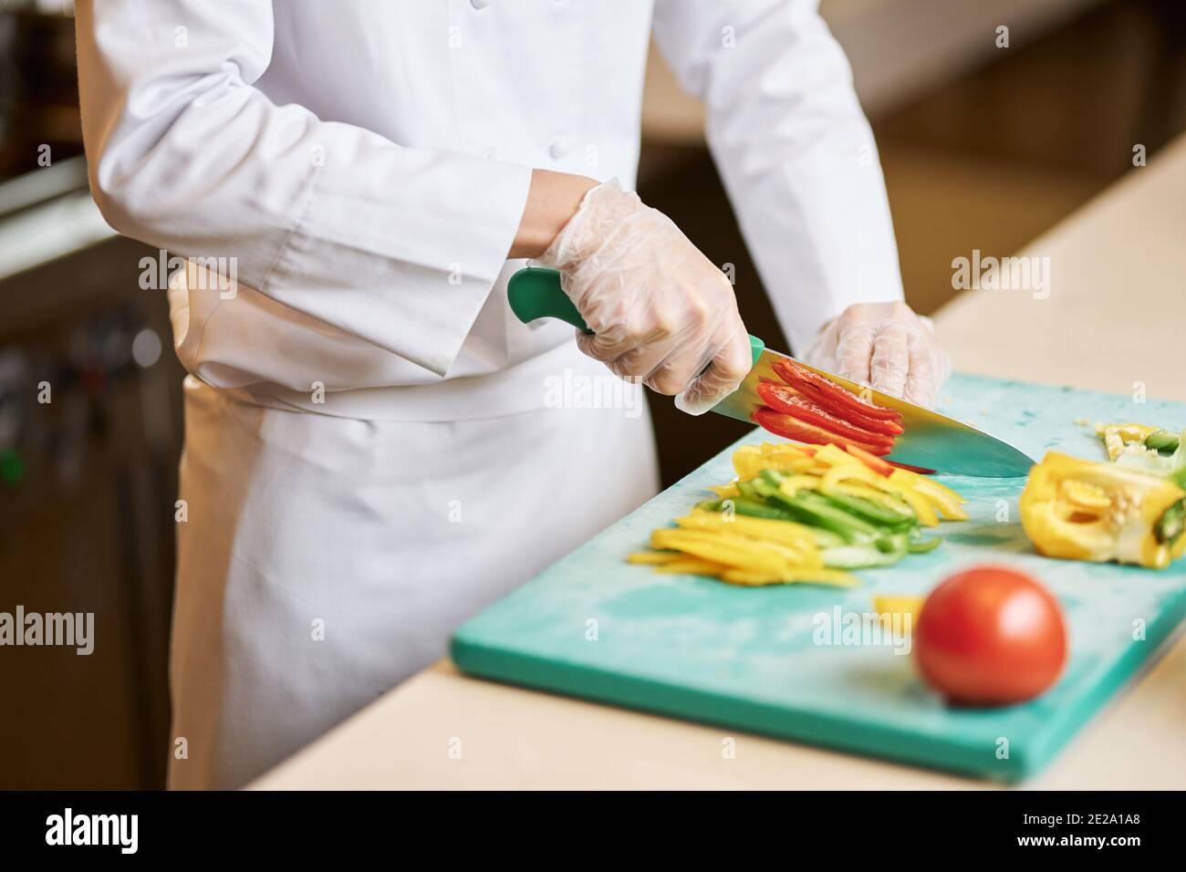 Cropped photo of chef in white uniform and clear gloves cutting peppers ...