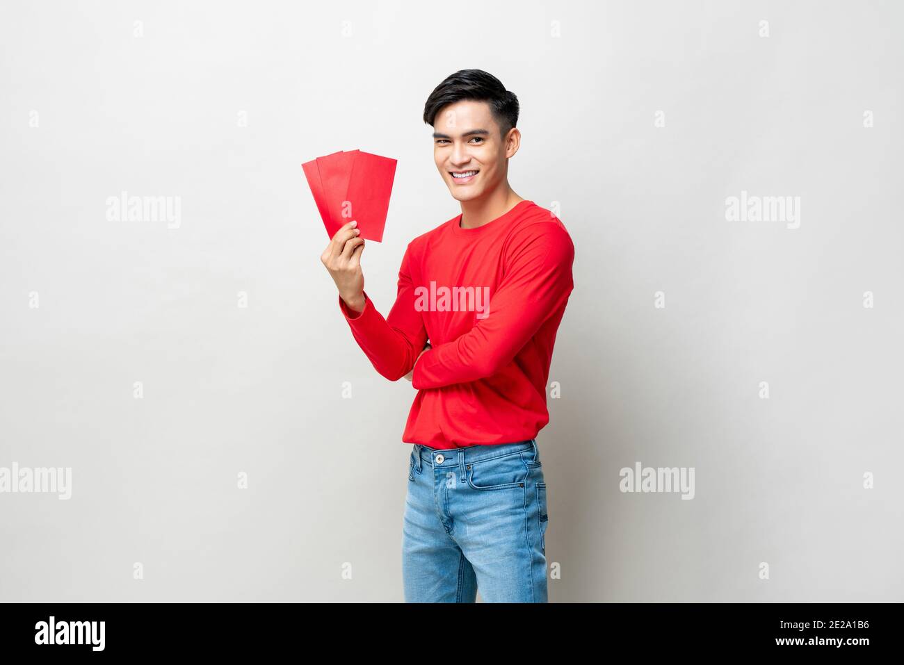 Smiling handsome Asian man holding red envelopes or Ang Pao in studio ...
