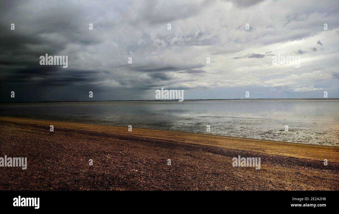 Dark grey storm clouds gather on a pebble beach on the Norfolk coast ...