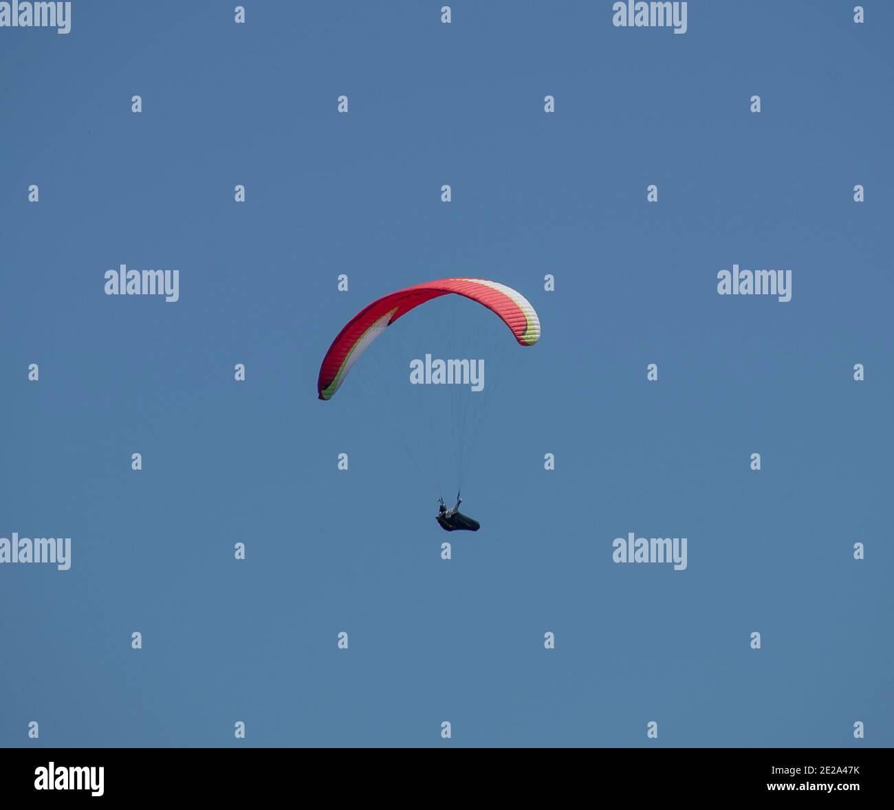 A single paraglider with a red and white canopy, against a clear, blue ...