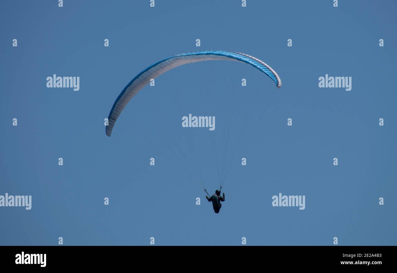 A single paraglider with a blue and white canopy, against a clear, blue ...