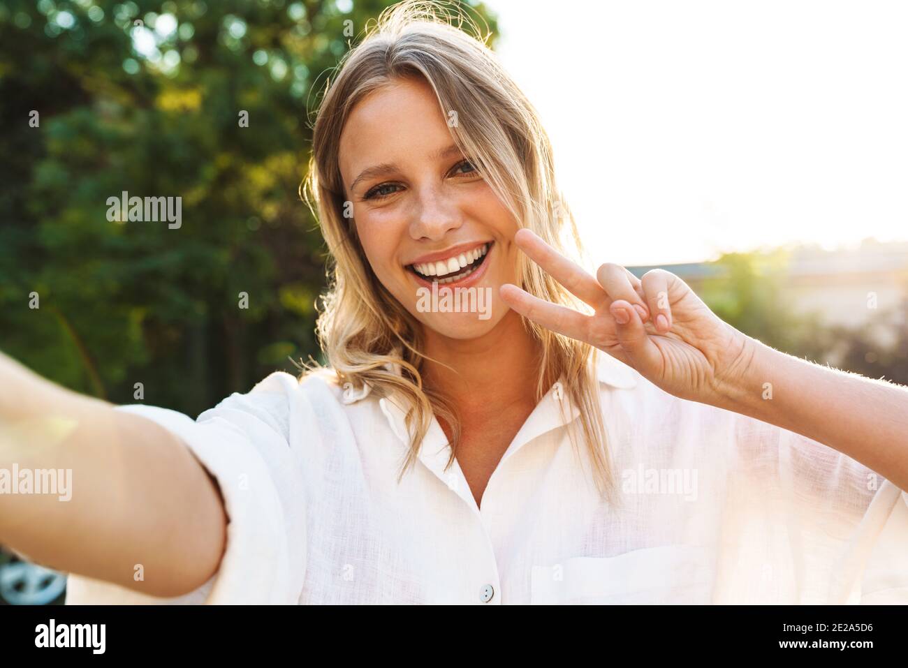 Beautiful happy woman gesturing peace sign and taking selfie while ...