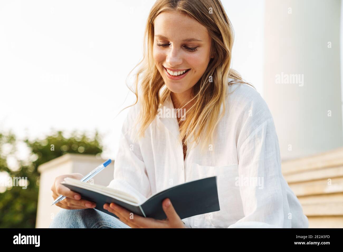 Beautiful happy student girl writing down notes in exercise book while ...