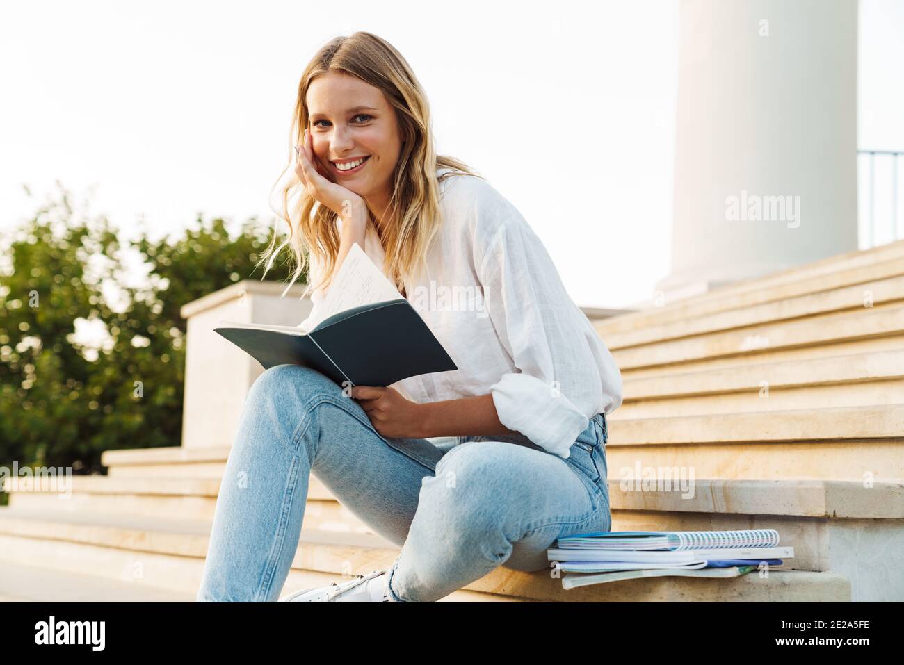 Beautiful happy student girl writing down notes in exercise book while ...