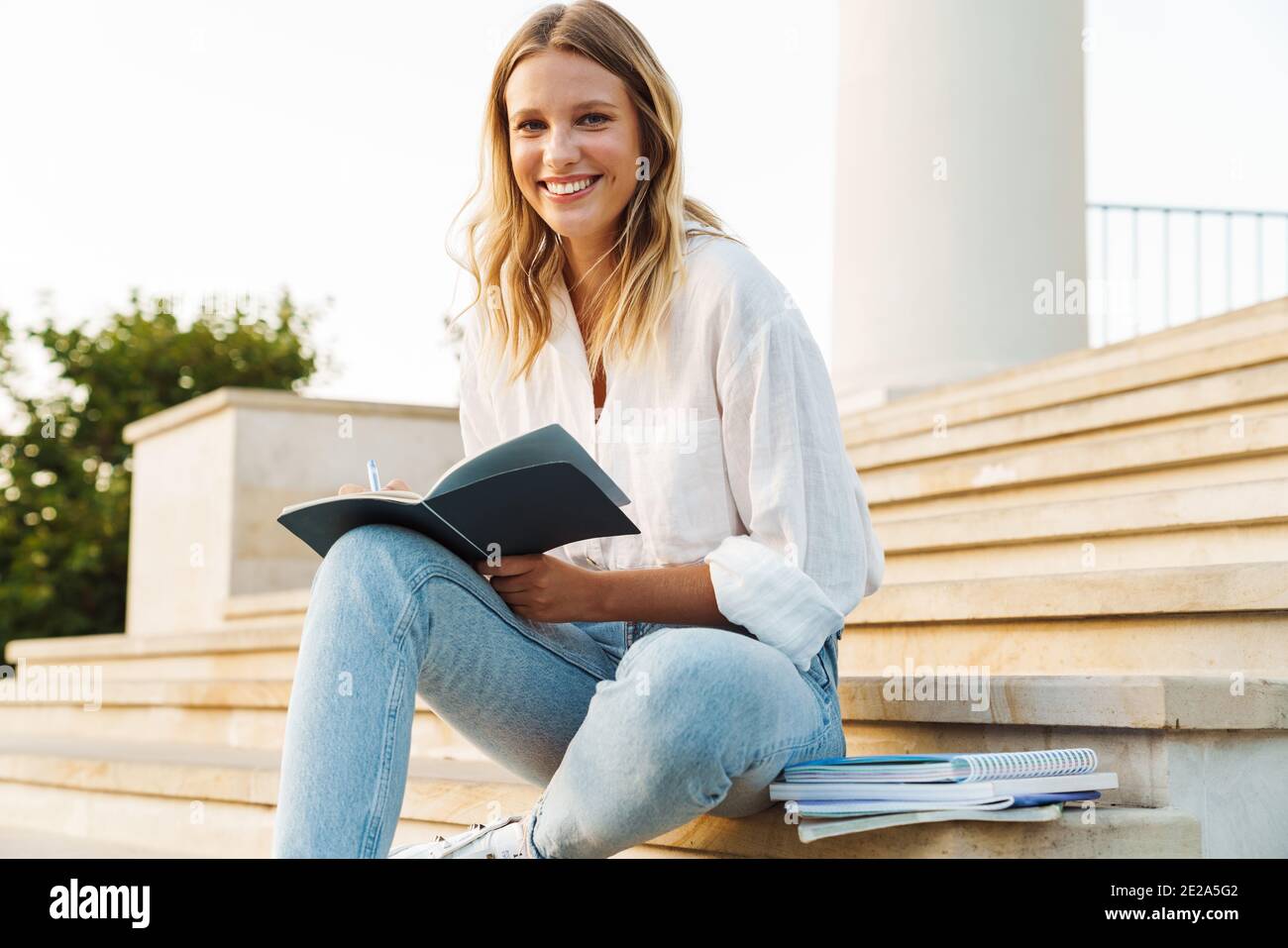 Beautiful happy student girl writing down notes in exercise book while ...