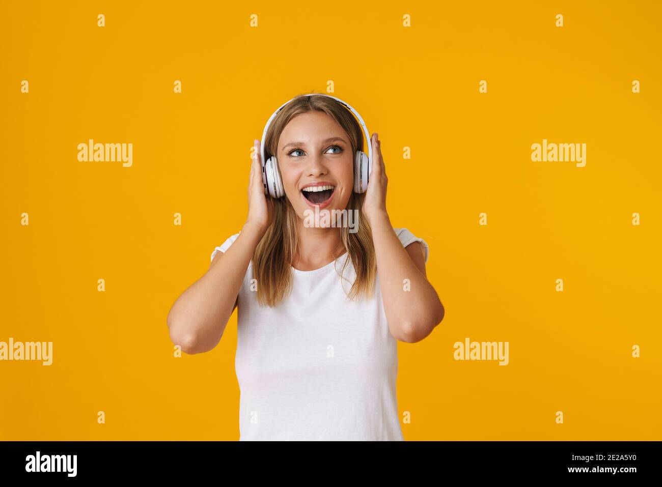 Excited blonde girl smiling while listening music with headphones ...