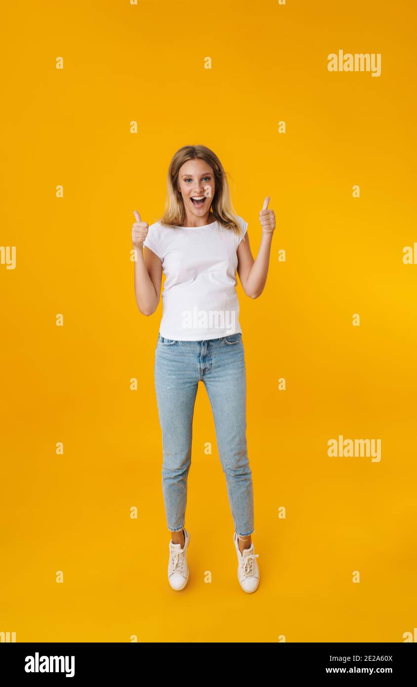 Excited beautiful girl jumping and showing thumbs up isolated over yellow background Stock Photo ...