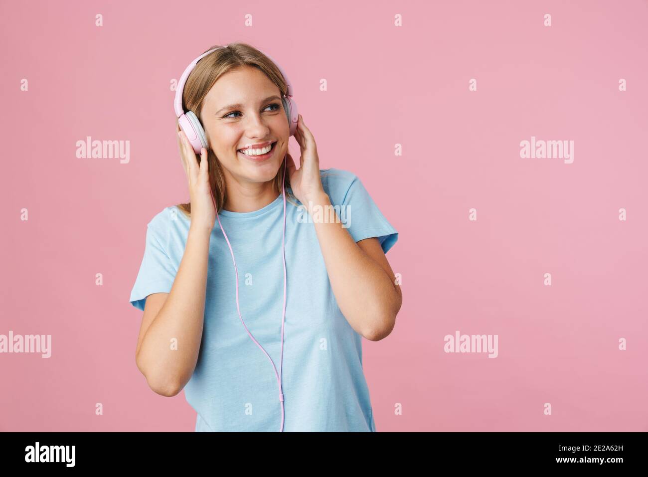 Cheerful blonde girl smiling while listening music with headphones ...