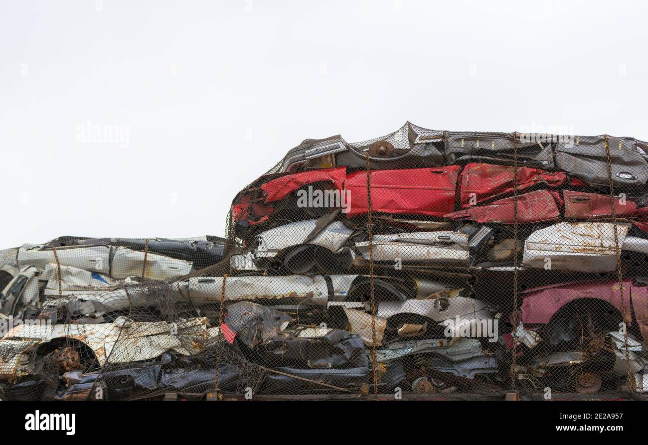 A pile of crushed cars held onto the back of a flat truck by a metal ...