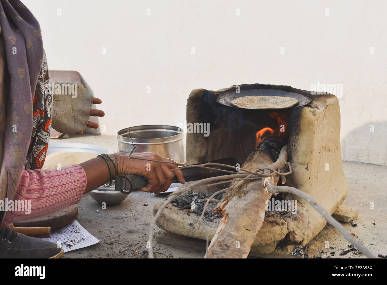 Rural Indian female preparing chapati in a traditional way on a wood ...