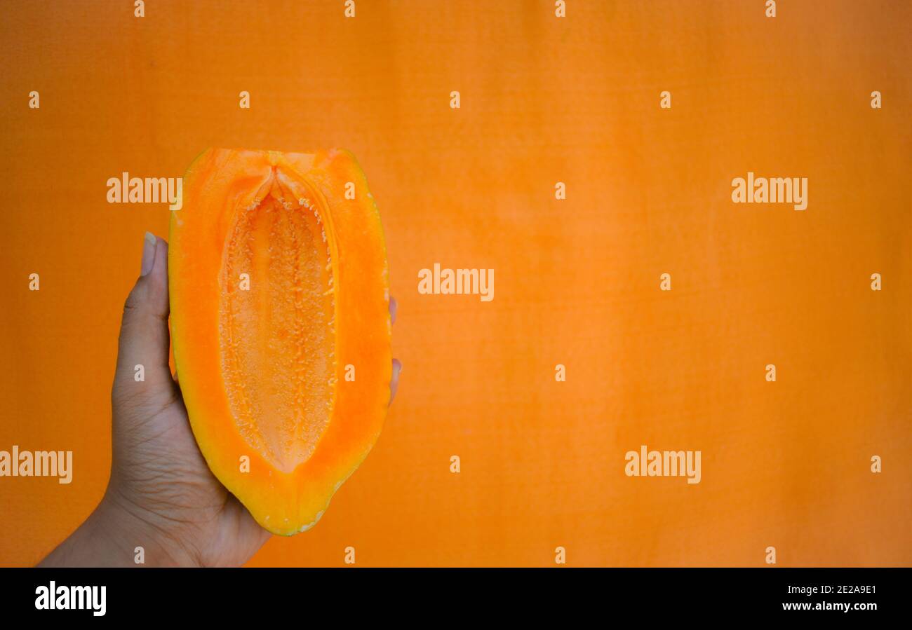 Hand holding half sliced papaya against an orange background Stock ...