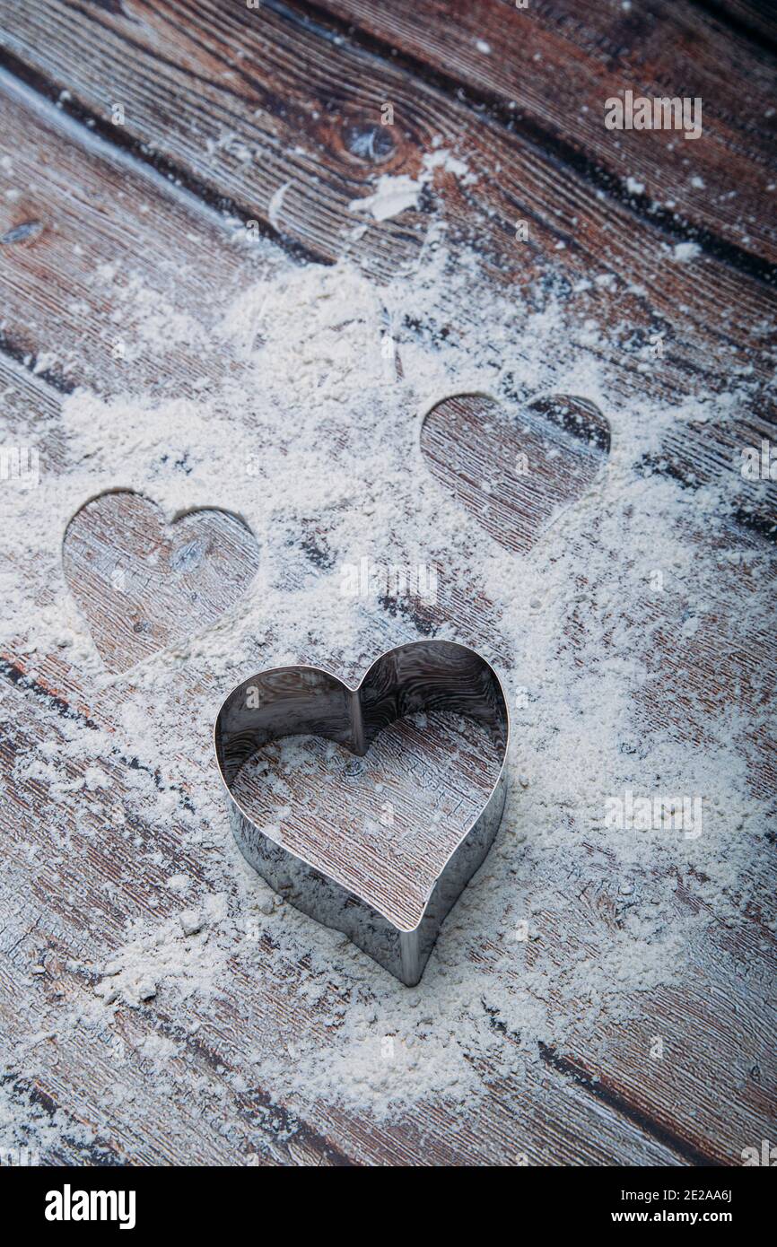 Vertical shot of a heart-shaped baking form and hearts on flour for ...