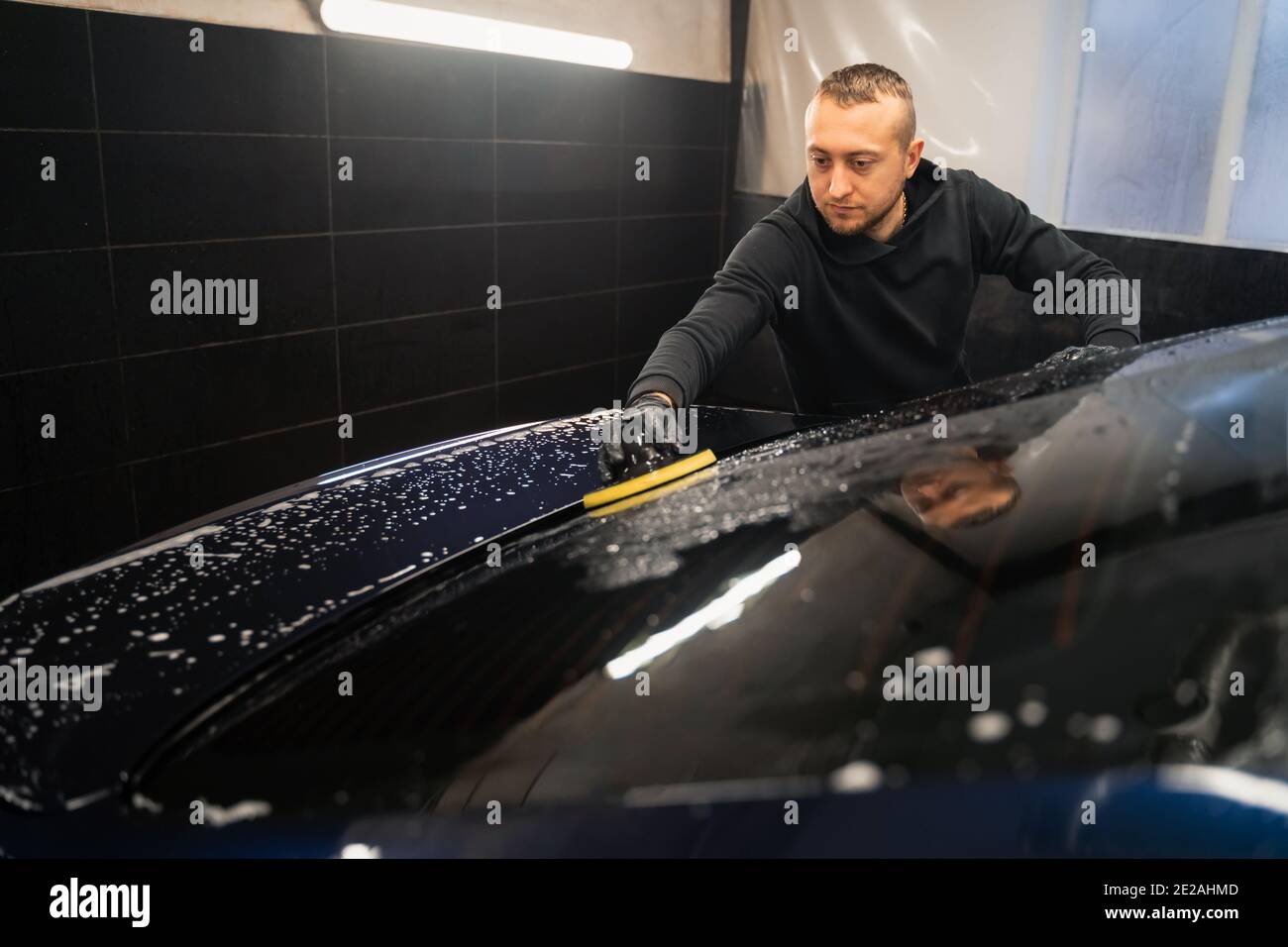 Man cleans rear window of car with circle sponge. Professional car wash ...