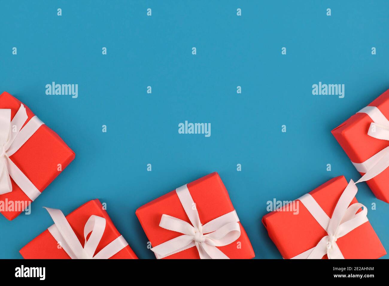 Small red gift boxes with white ribbons at bottom of blue background ...