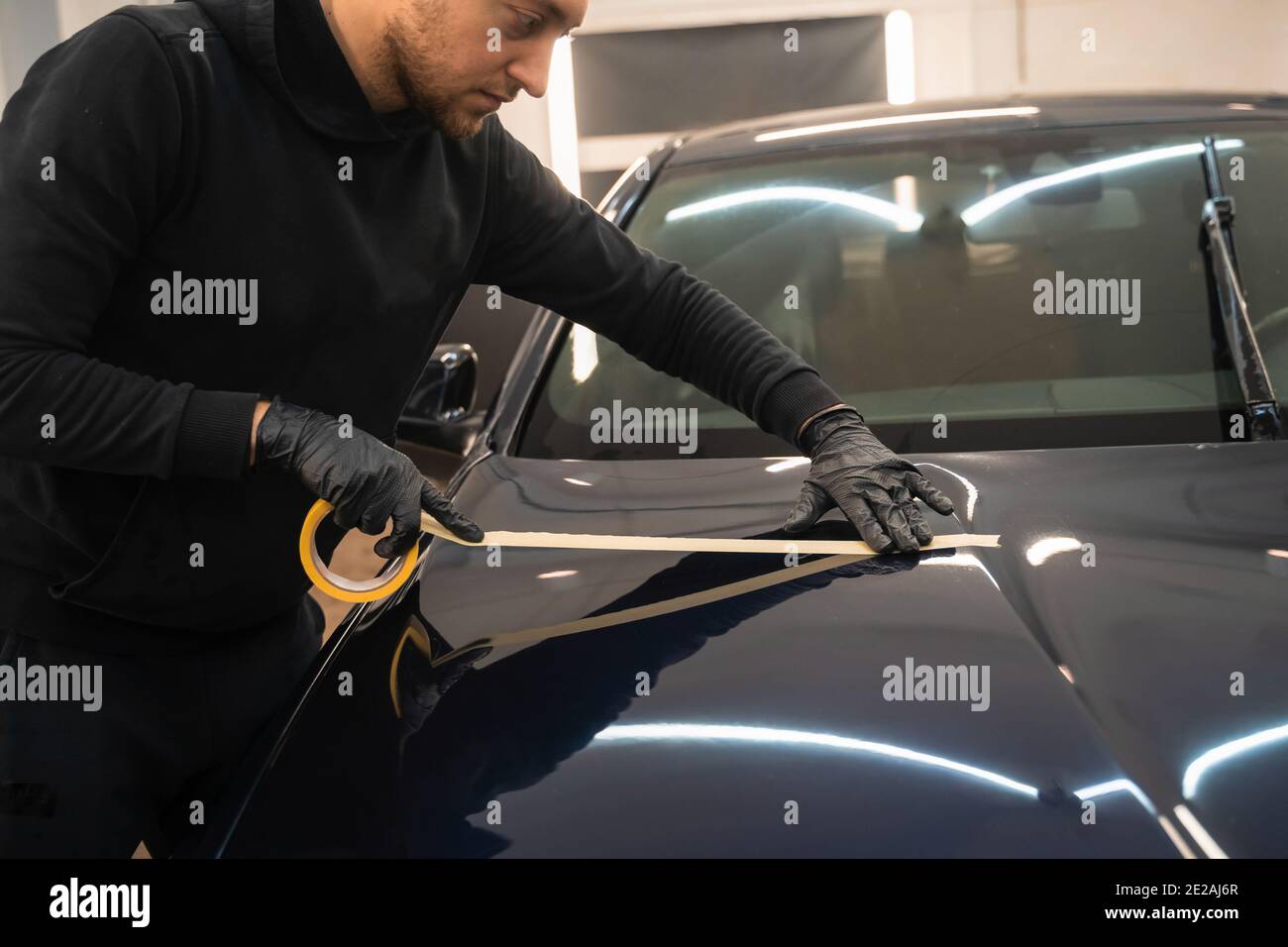 Auto detailing worker pasting protective tape on the car hood before ...