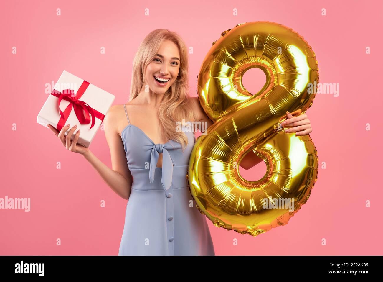 Joyful millennial lady in pretty dress holding wrapped gift and golden ...