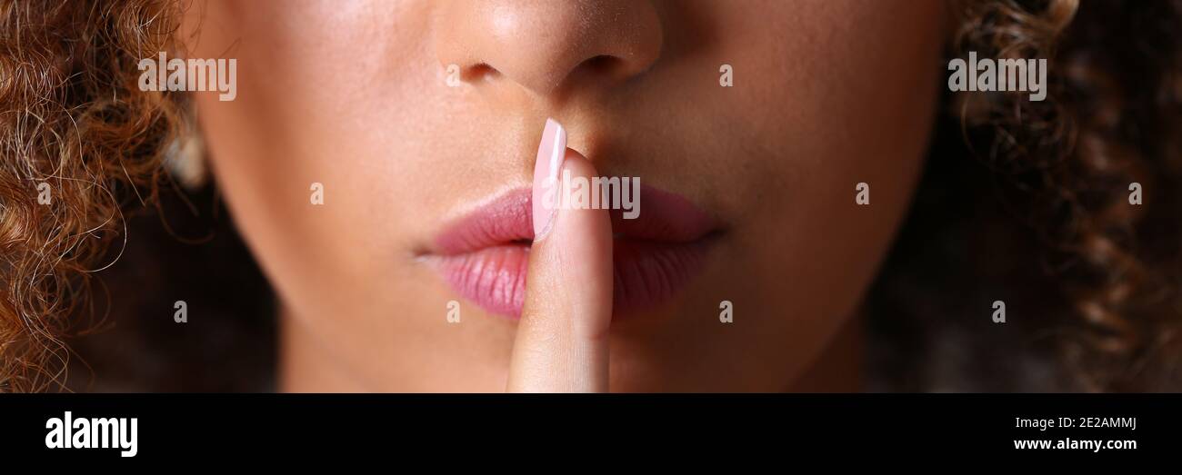 Curly young woman holding index finger at lips Stock Photo - Alamy