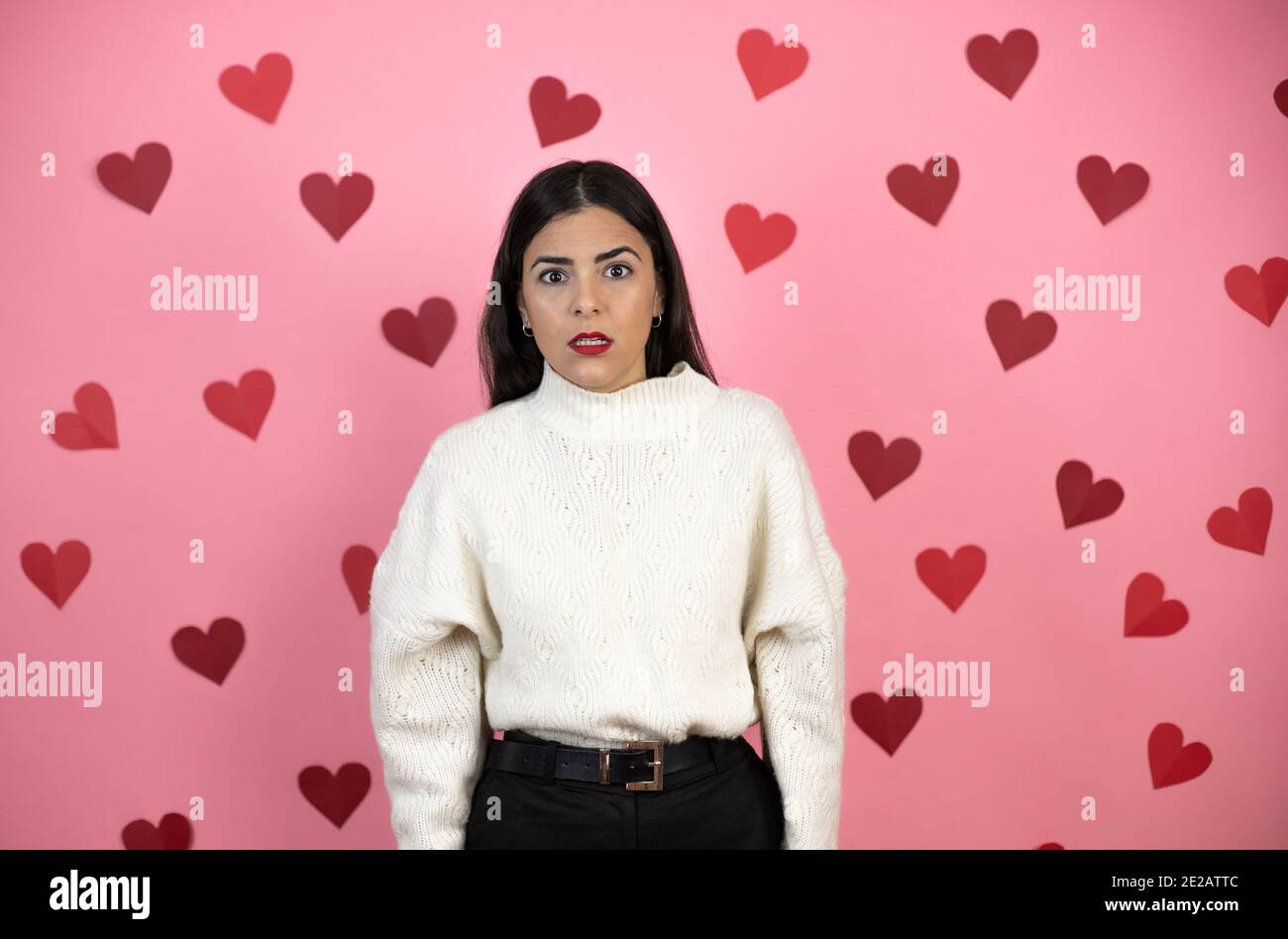 Young beautiful woman over pink background with harts afraid and ...