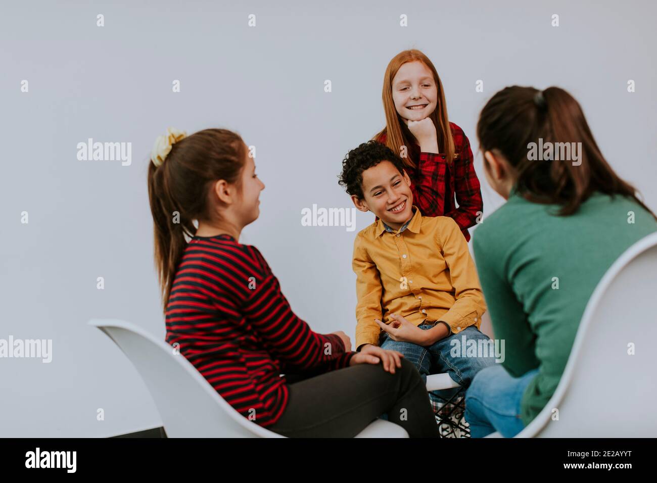 Portrait of cute little kids in jeans talking and sitting in chairs ...