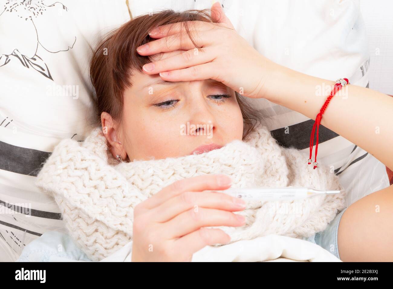 a young pretty girl is sick at home in bed, holds her hot forehead and ...