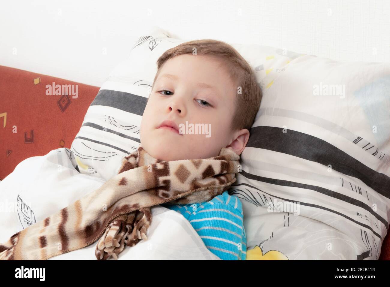 sick child boy in a blue sweater with a scarf in bed waiting for ...