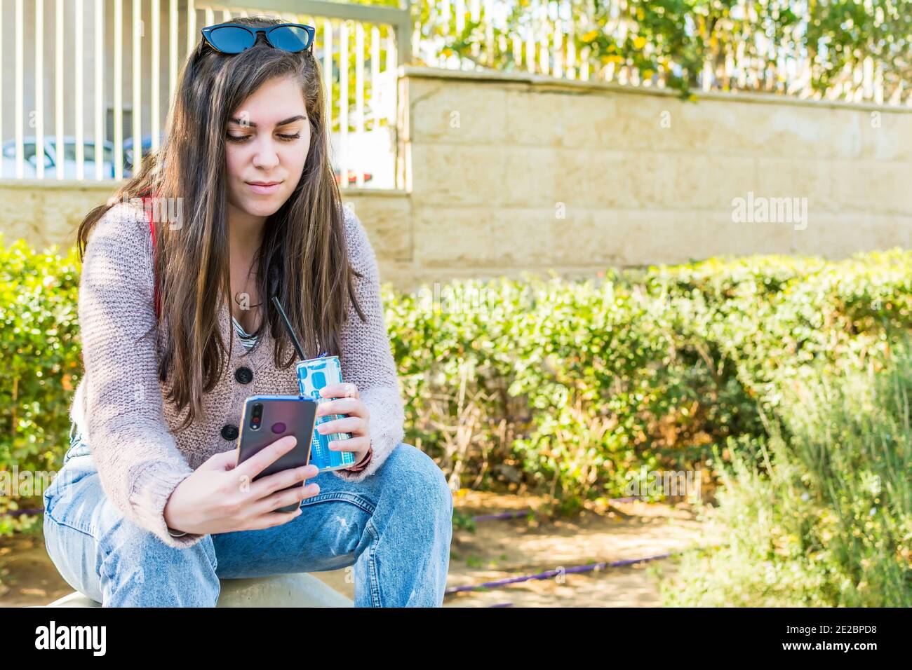 Side view of a smiling female using a smartphone with soda sitting down ...