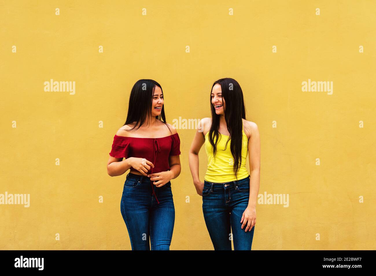 Happy hispanic friends standing against a yellow wall smiling and ...