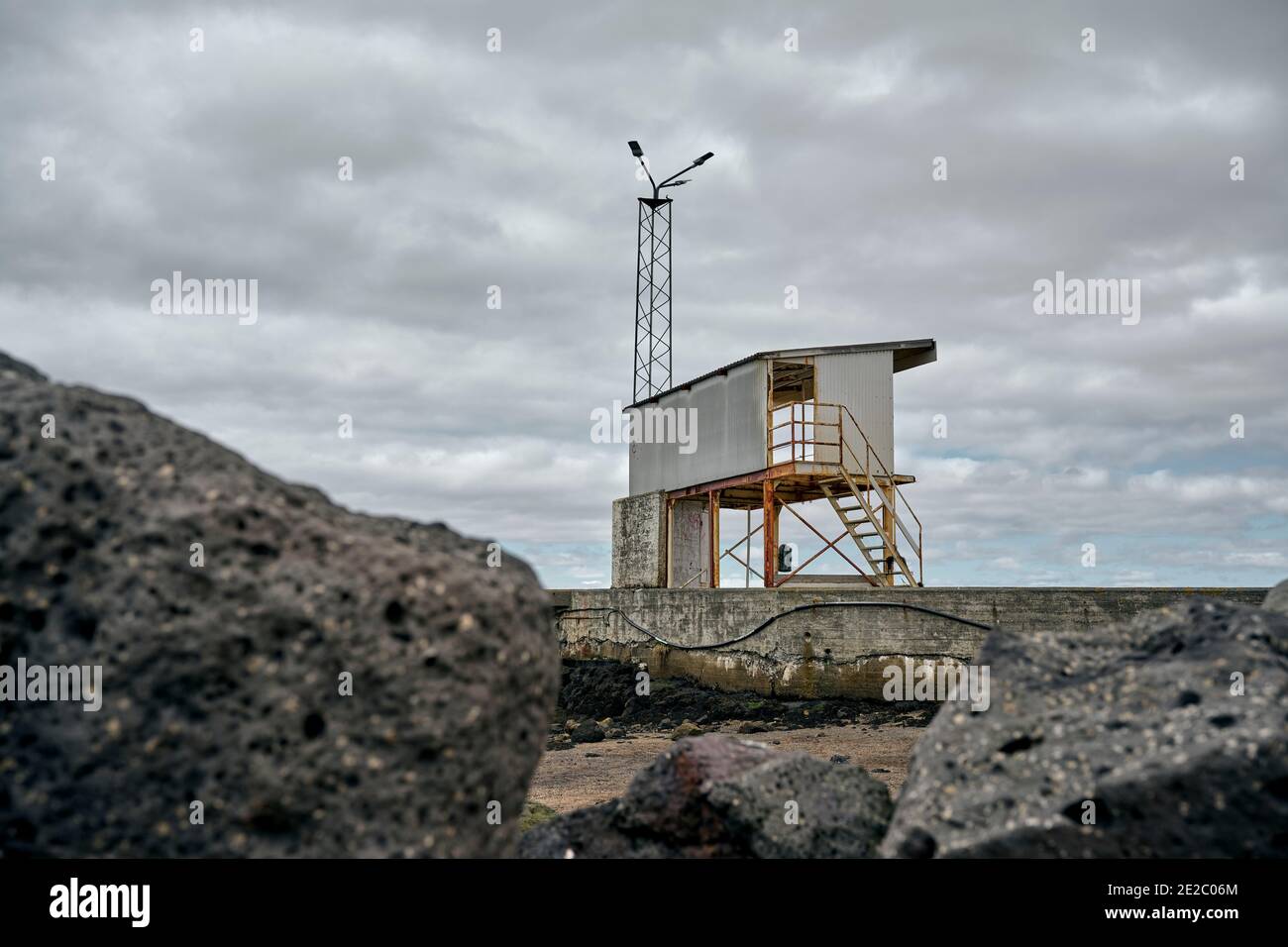 Rough stones and cement building located on seashore against cloudy sky ...