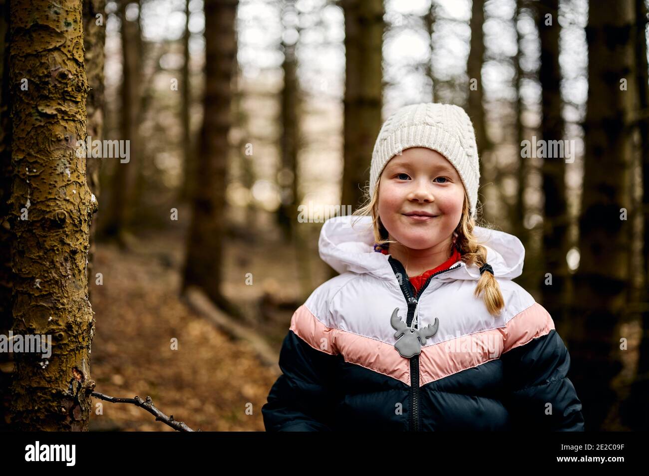Happy kid with braid in warm clothes and hat smiling and looking at ...
