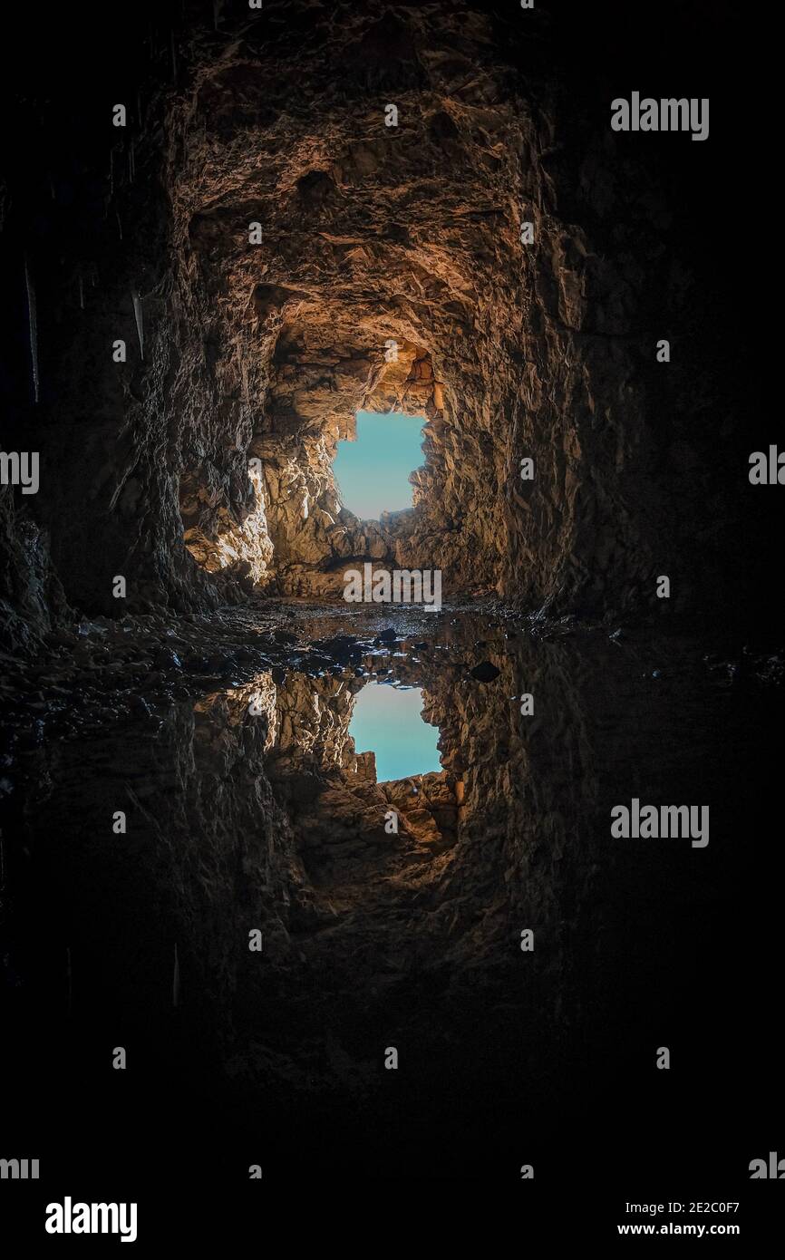 Vertical shot of a stone cave entrance reflecting in water inside Stock ...