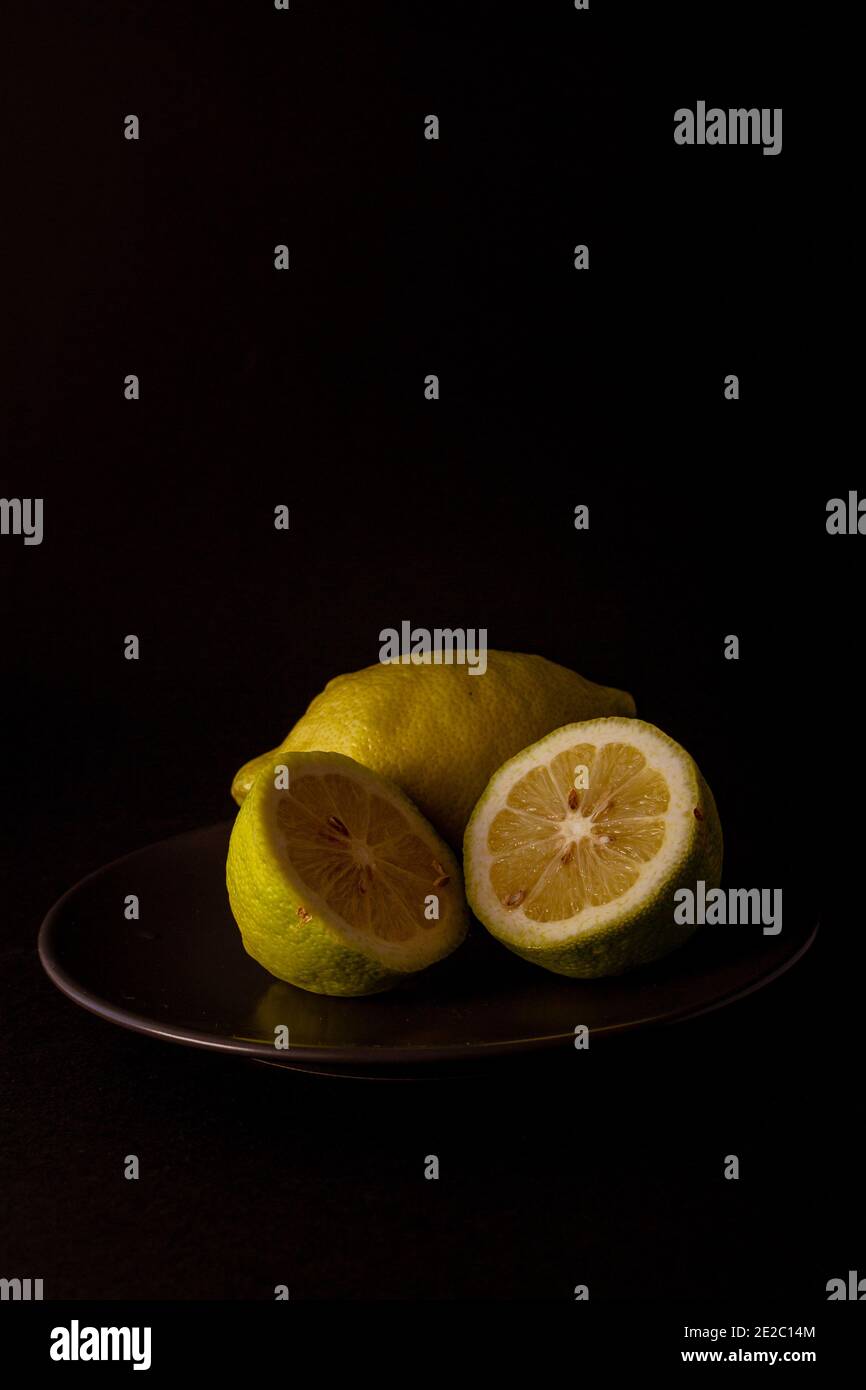Vertical closeup of a black plate of whole and cut lemons isolated in ...