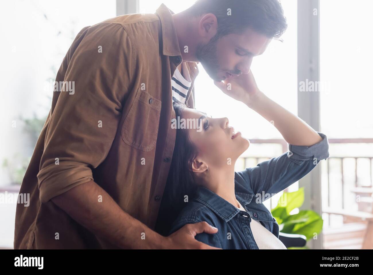 side view of young man bending over seductive woman touching his face ...