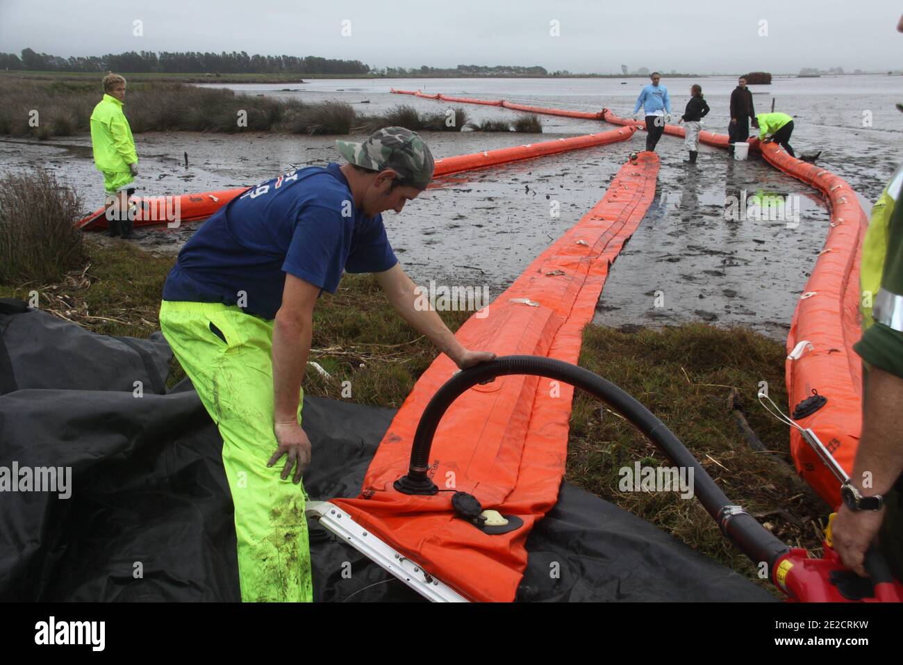 Workers construct oil booms at Maketu Estuary in Tauranga, New Zealand ...