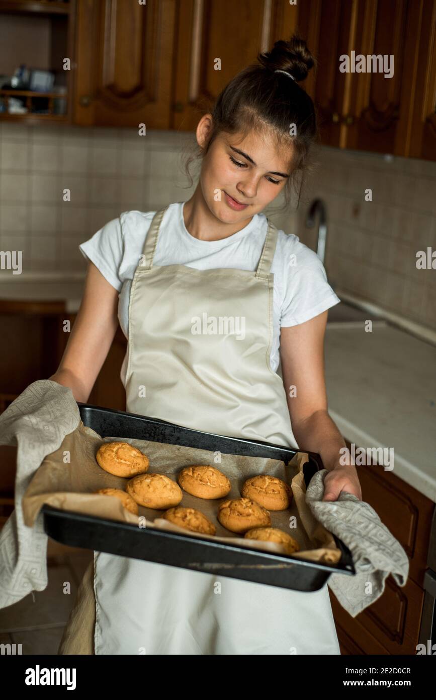 Vertical portrait Smiling teen girl taking cookies out of the oven ...