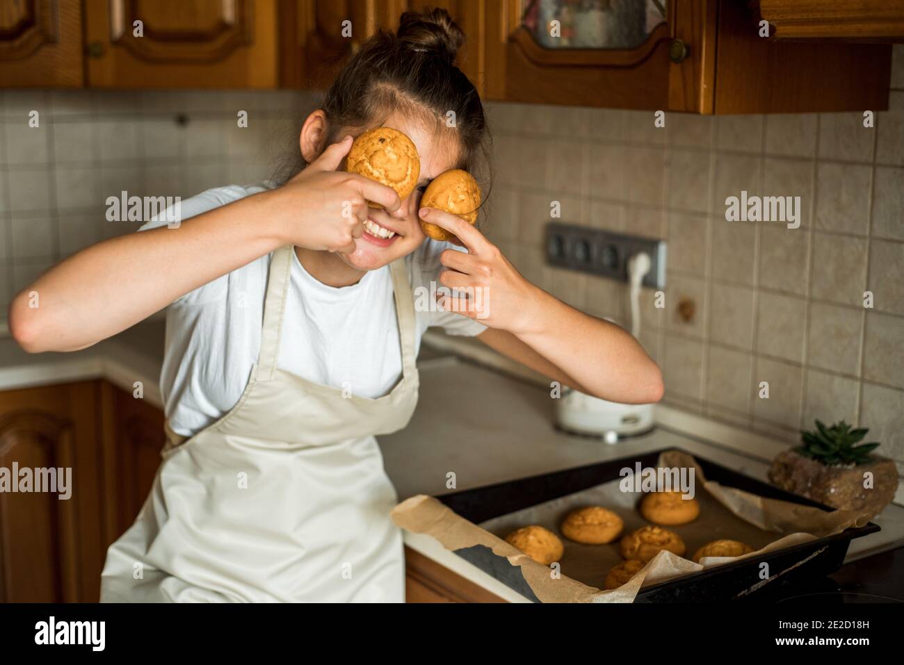Smiling teen girl taking cookies out of the oven in the kitchen ...