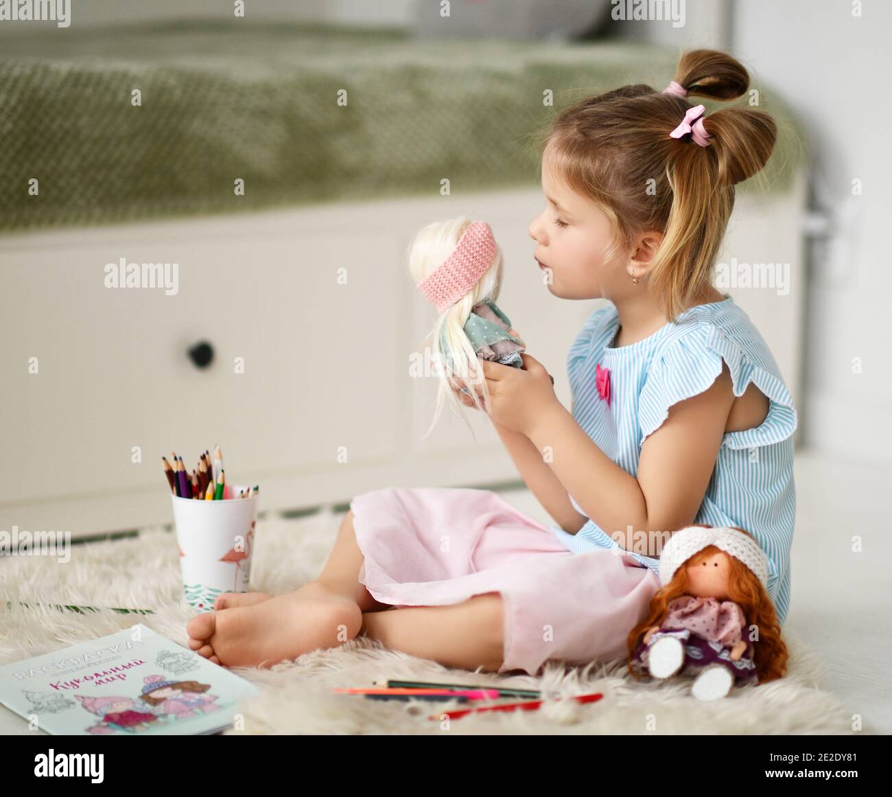 Pretty small girl in home clothing sitting, playing with dolls and ...