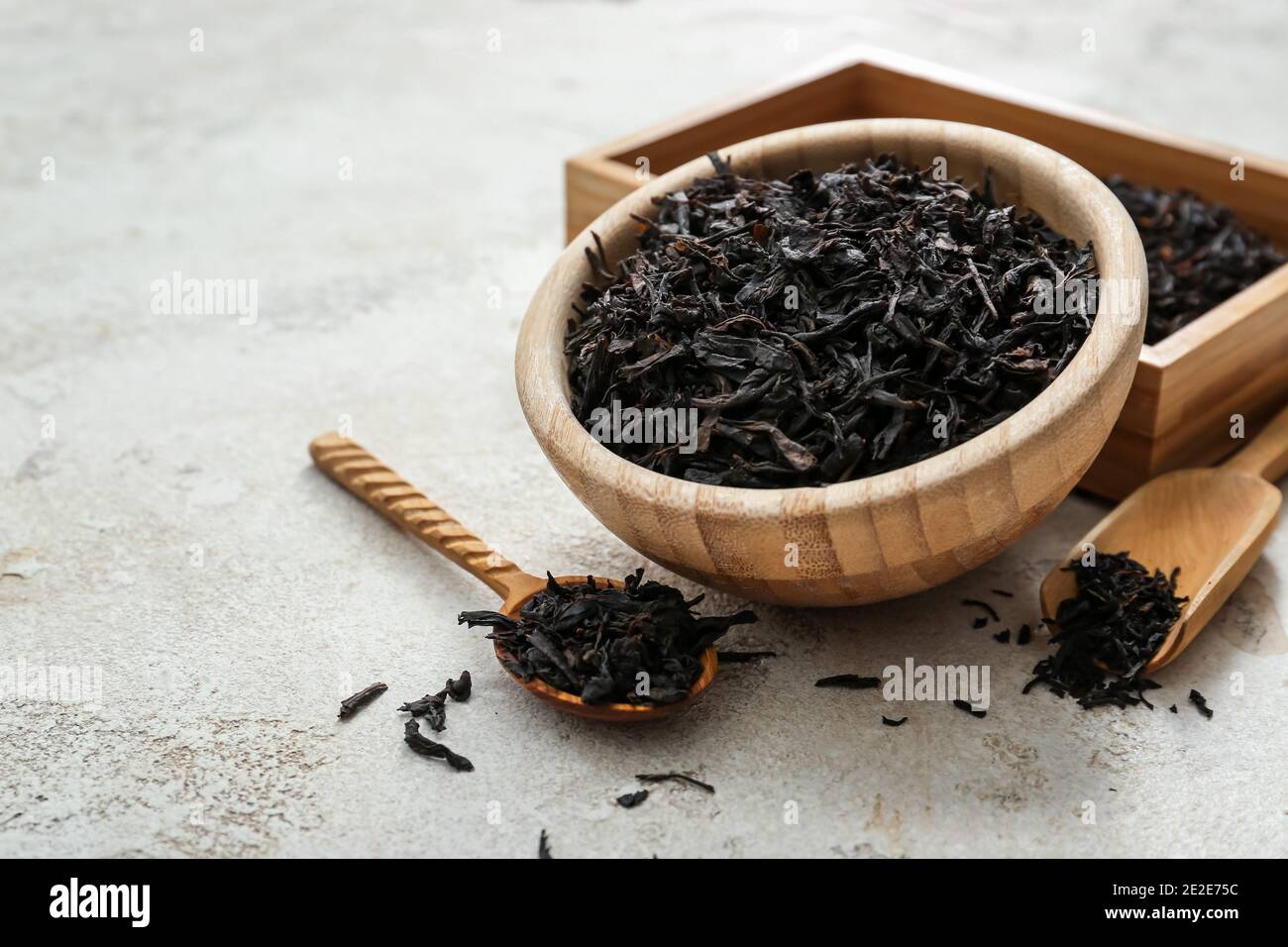 Dry black tea leaves in bowl with spoon on light background Stock Photo ...
