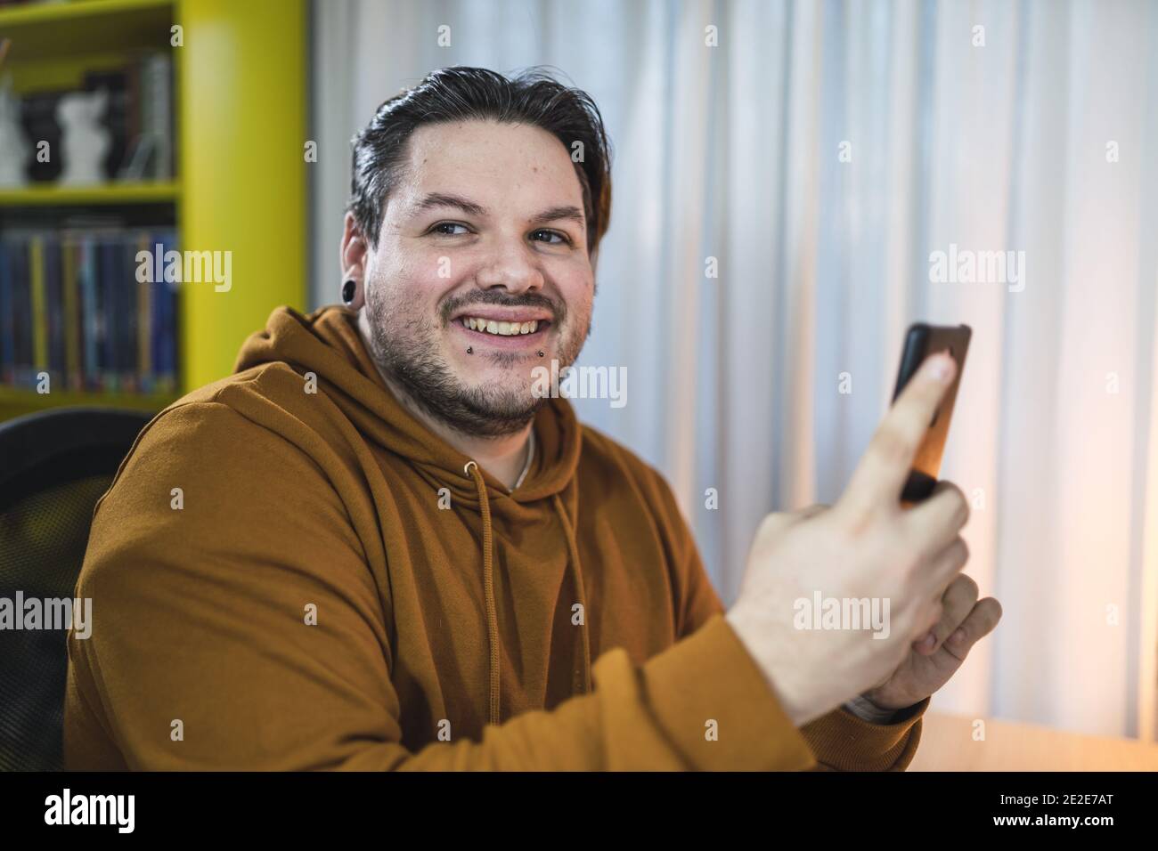 Selective focus shot of a cheerfu cool guy with piercings sitting in a ...