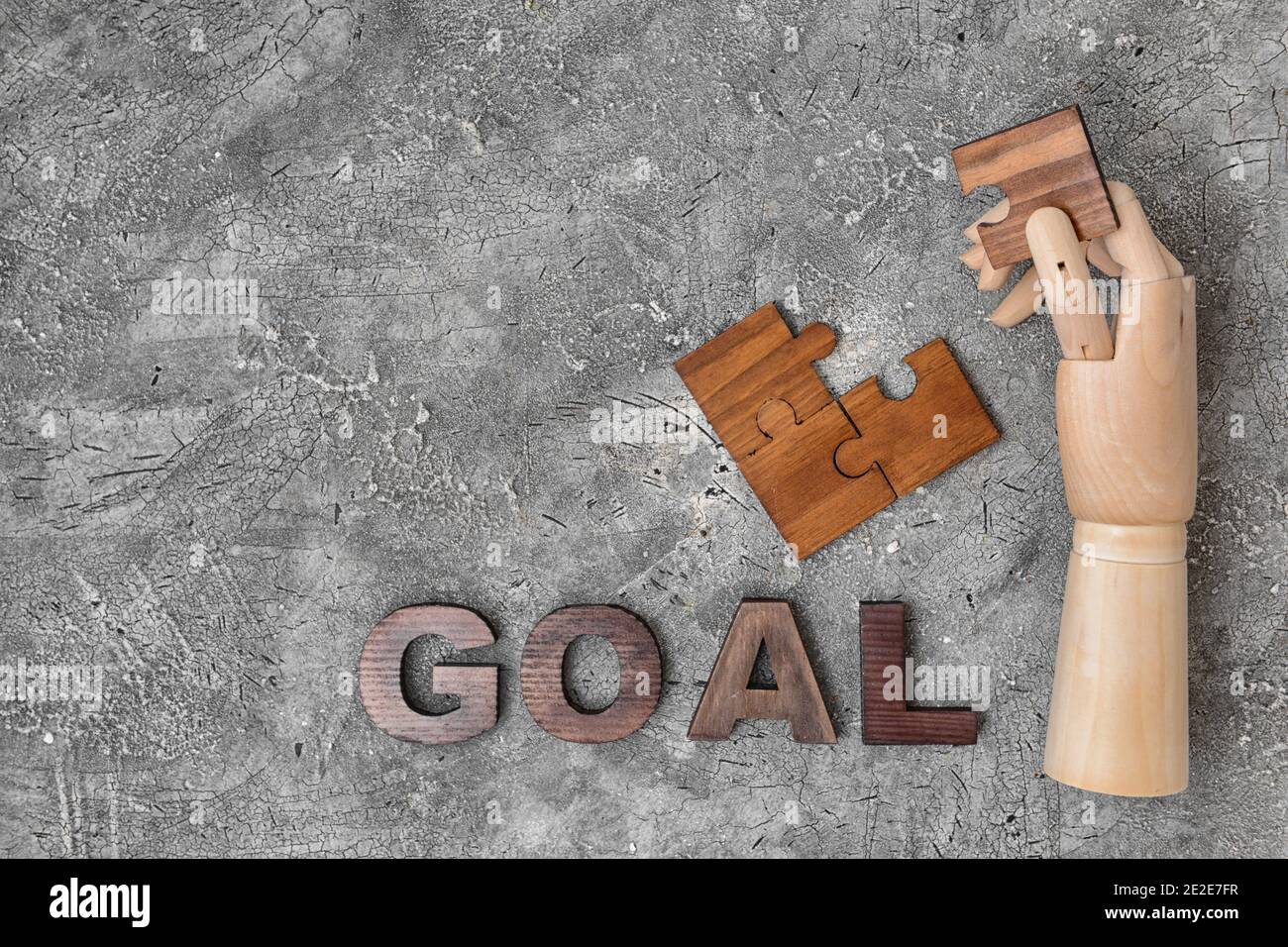 Wooden human hand with puzzle pieces and word GOAL on dark background ...